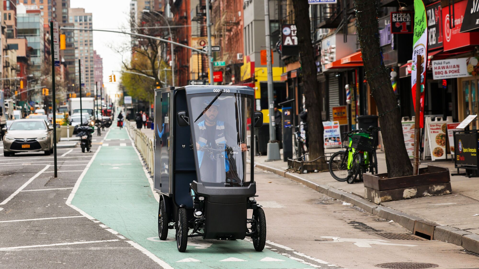 Small enclosed electric vehicle on green bike lane in busy city street 